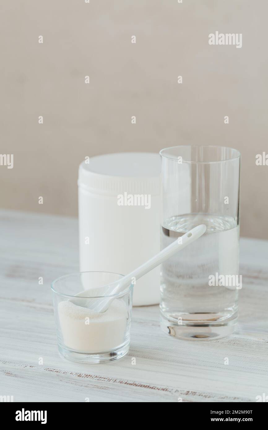 Collagen powder in bowl, glass of water and measure spoon on a white ...