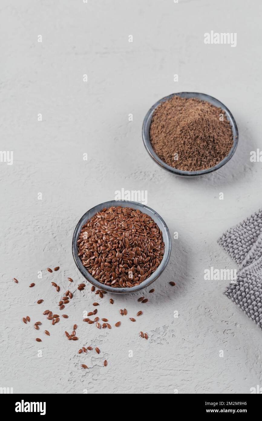 Brown flax seed and ground or crushed flaxseed or linseed in small bowl on a light gray ...