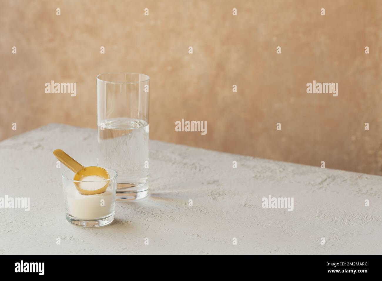 Collagen powder in bowl, glass of water and measure spoon on a white ...