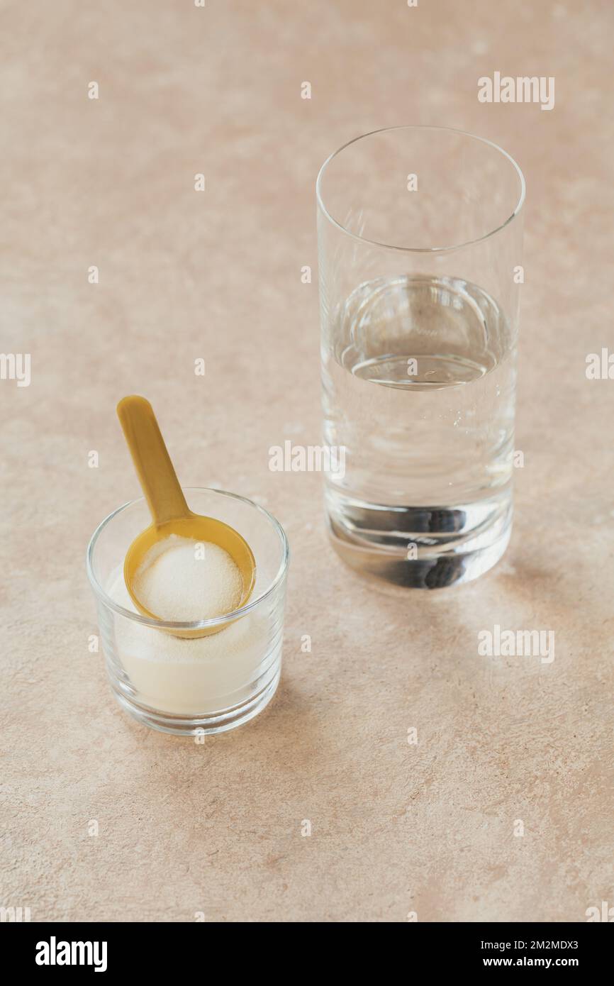 Collagen powder in bowl, glass of water and measure spoon on a light ...