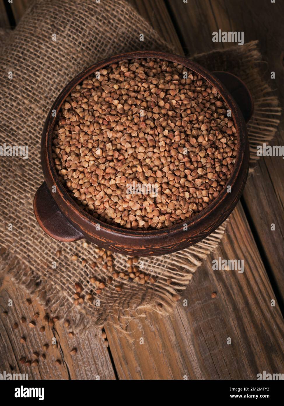 Organic uncooked scattered buckwheat grain in a bowl on a rustic wooden ...
