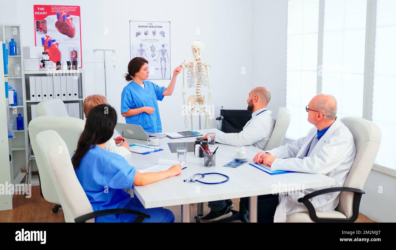 Young female assistent pointing on skeleton in front of medical ...