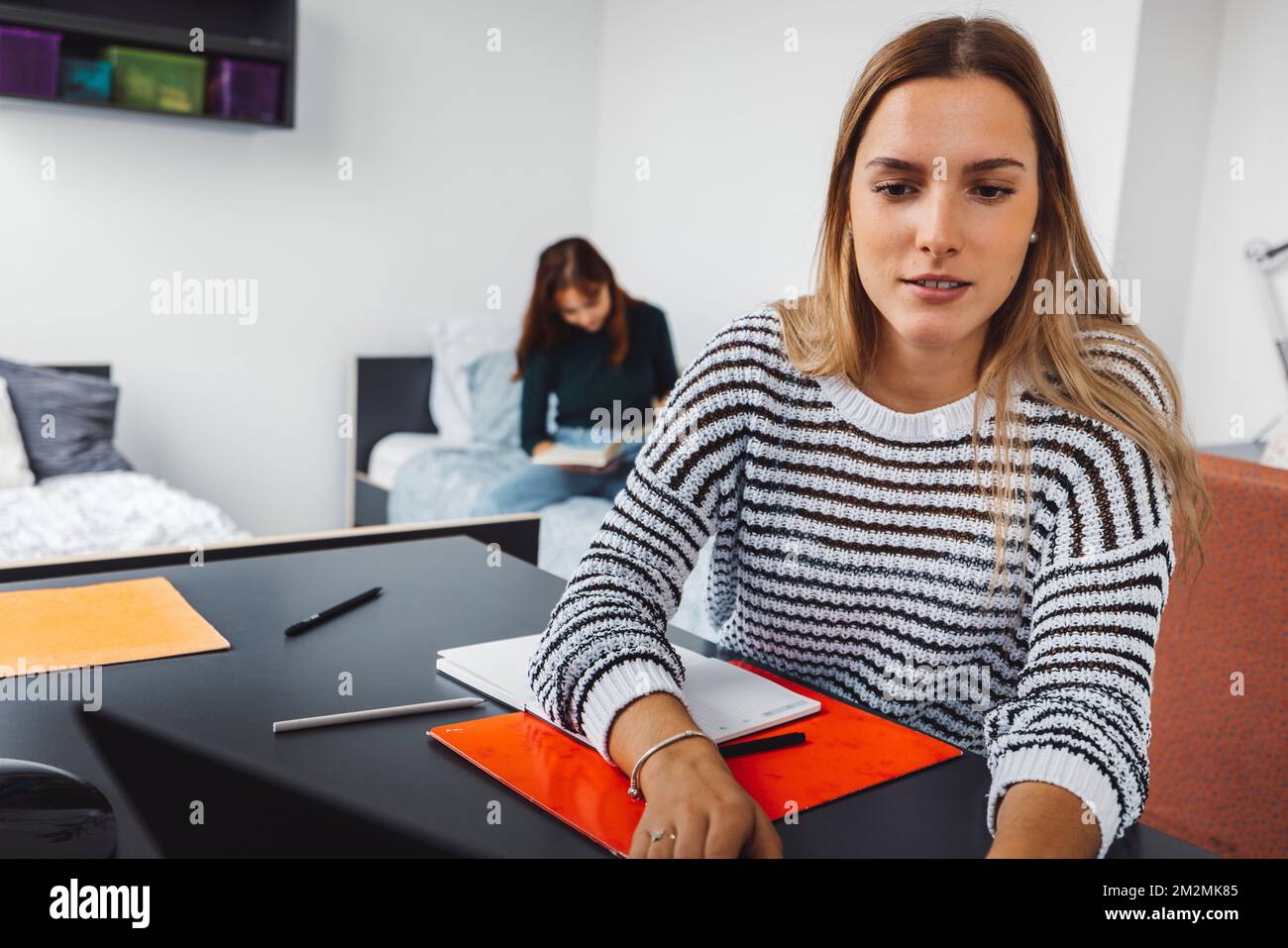 Blonde woman, student, studying in her dorm room, her roommate sitting ...