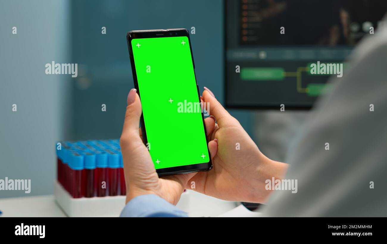 Close up of doctor's hand holding phone with green screen sitting at ...