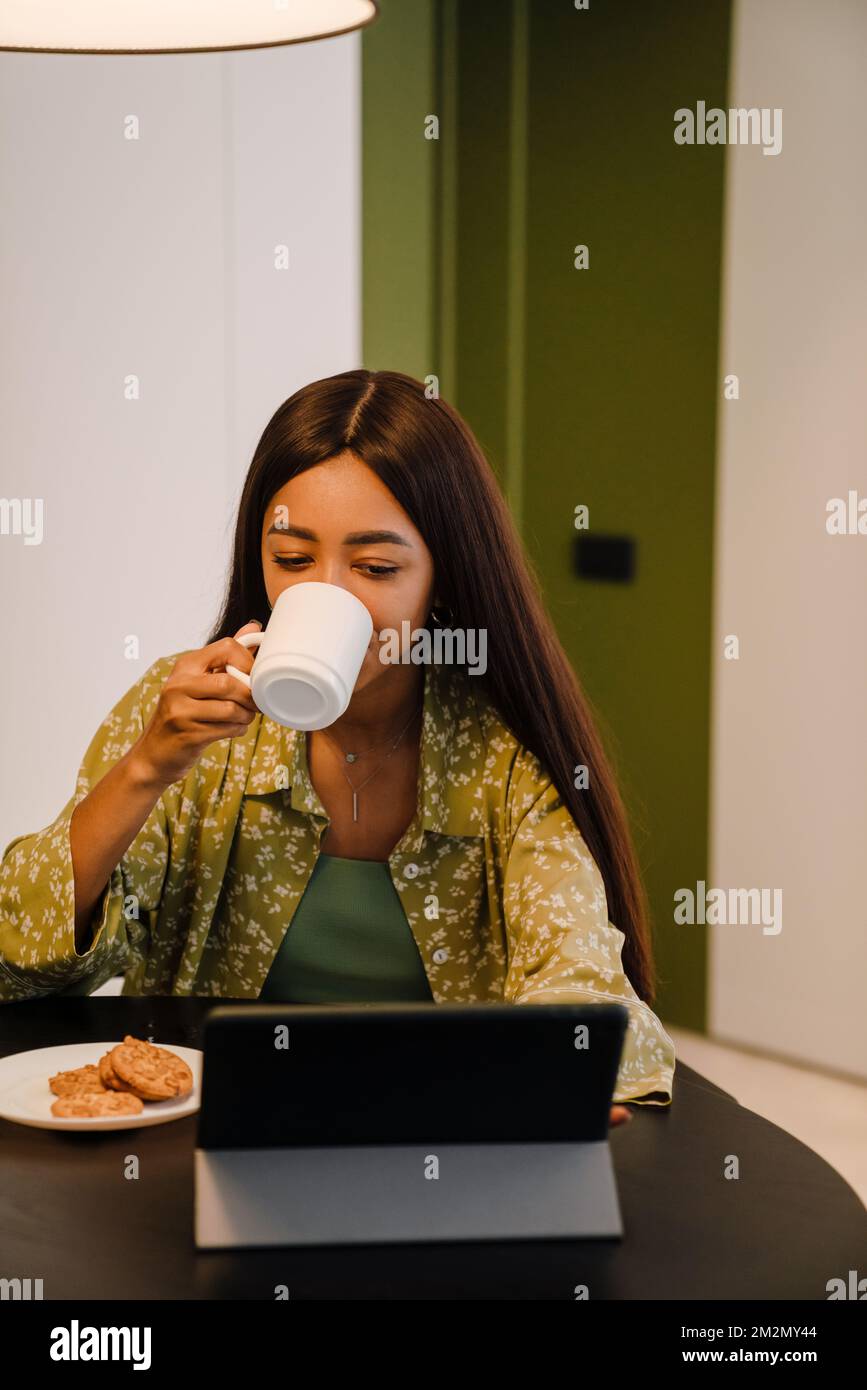 Young beautiful long-haired woman drinking coffee with cookies and ...