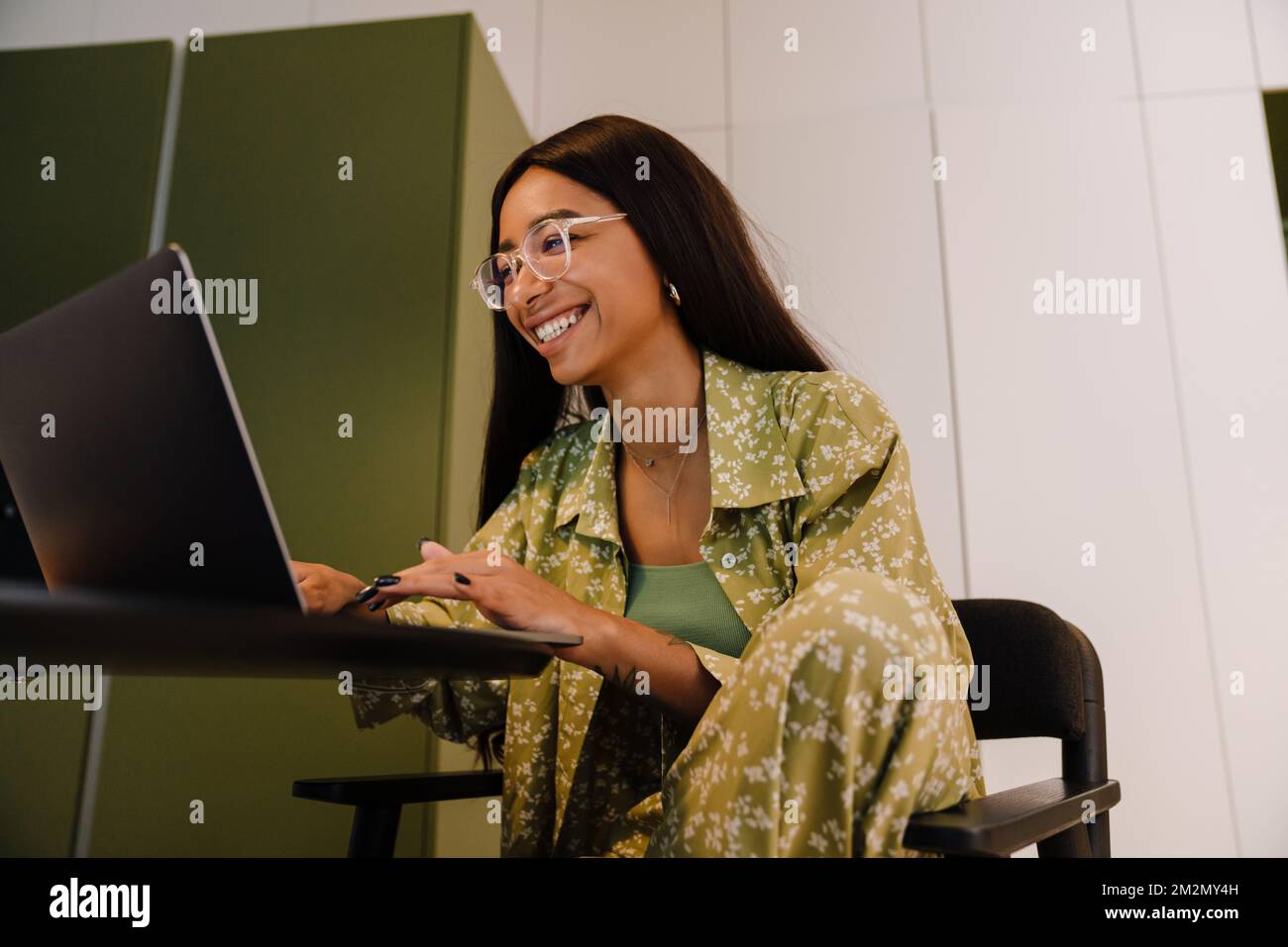 Young beautiful smiling long haired woman in glasses working on laptop ...