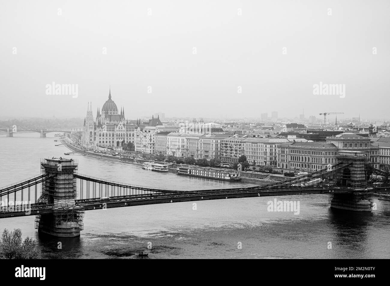 A grayscale of the Szechenyi Chain Bridge on a foggy day in Budapest ...