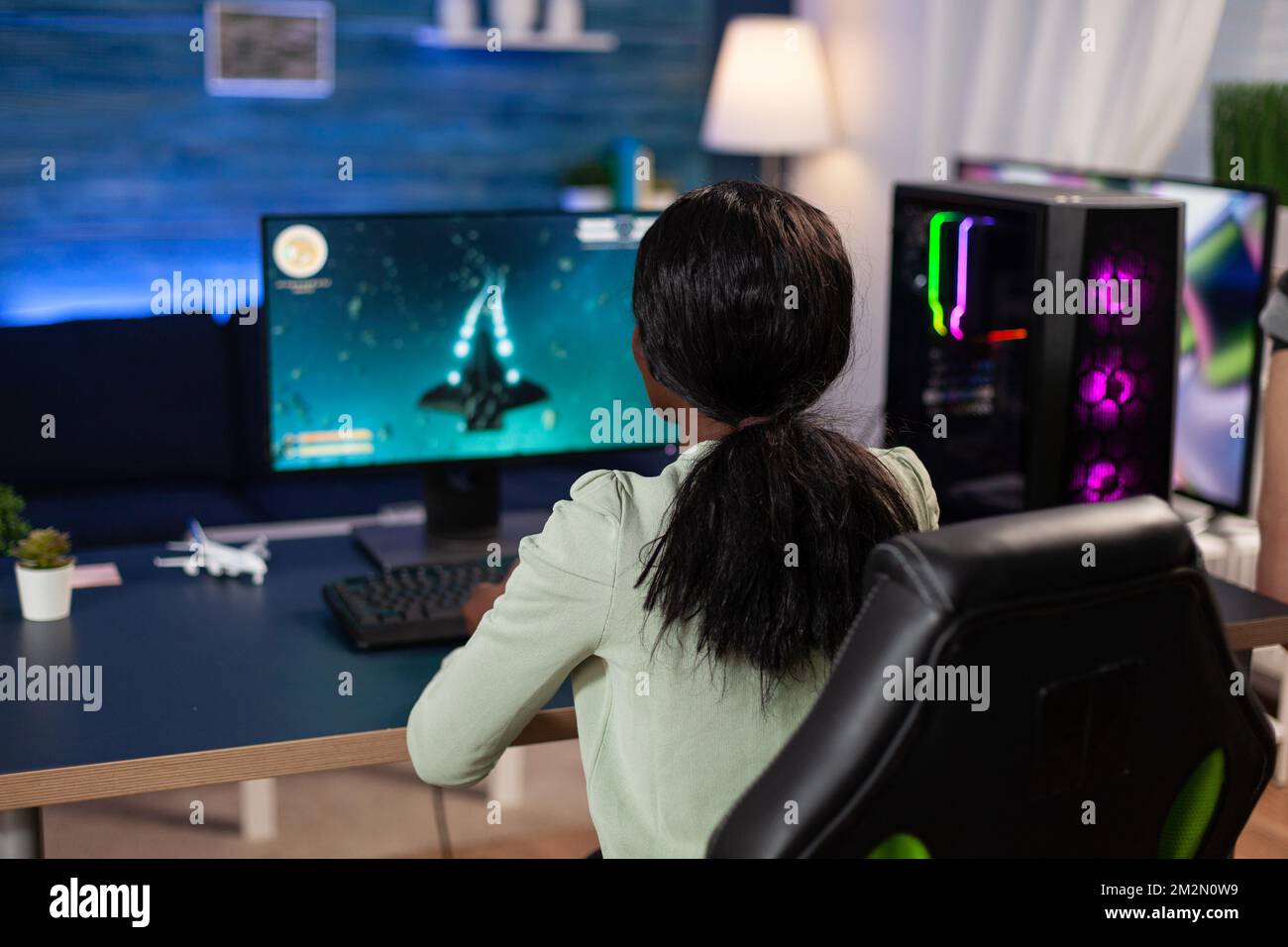 Pro gamer woman sitting at gaming desk playing space shooter videogames ...