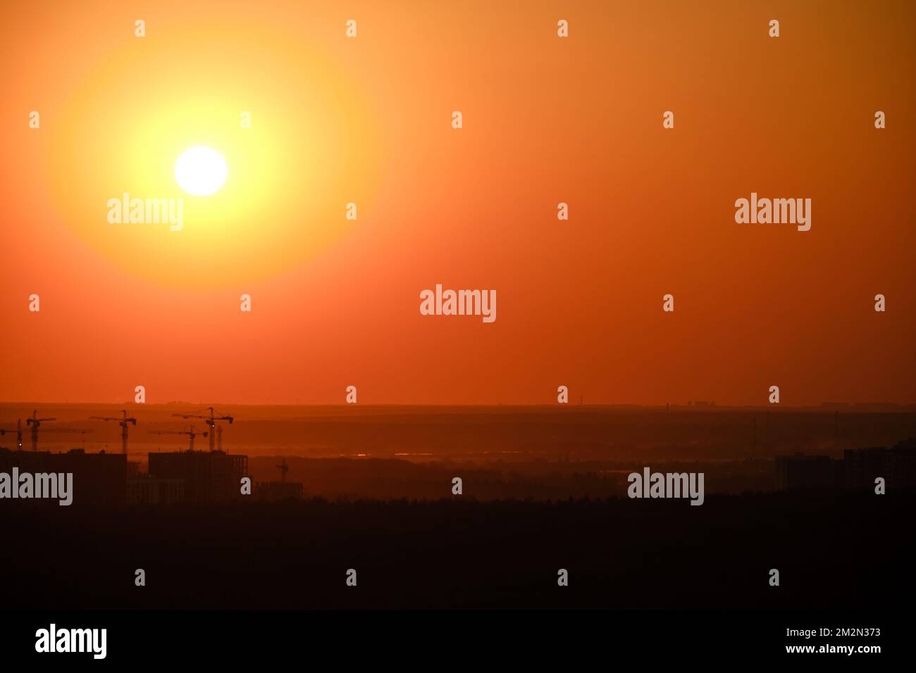 A big red sun in the sunset sky over the roofs of buildings, urban ...