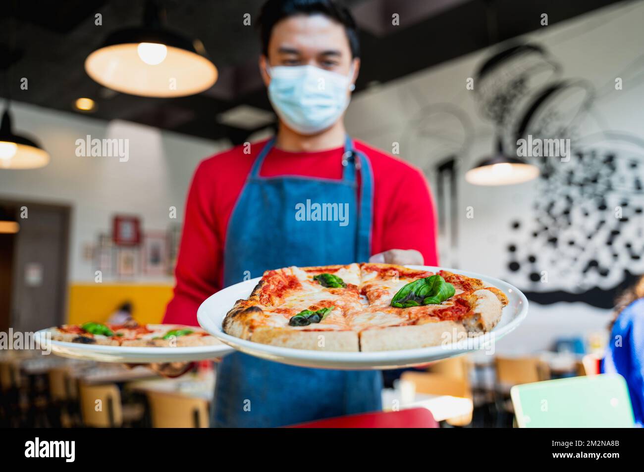 Unrecognizable waiter with face mask serving Italian pizza margherita ...