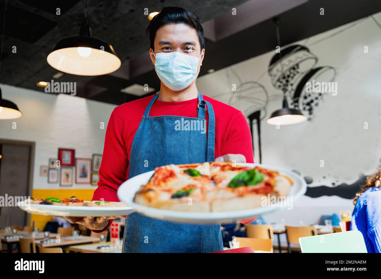 Portrait of young smiling waiter with protective face mask serving and ...