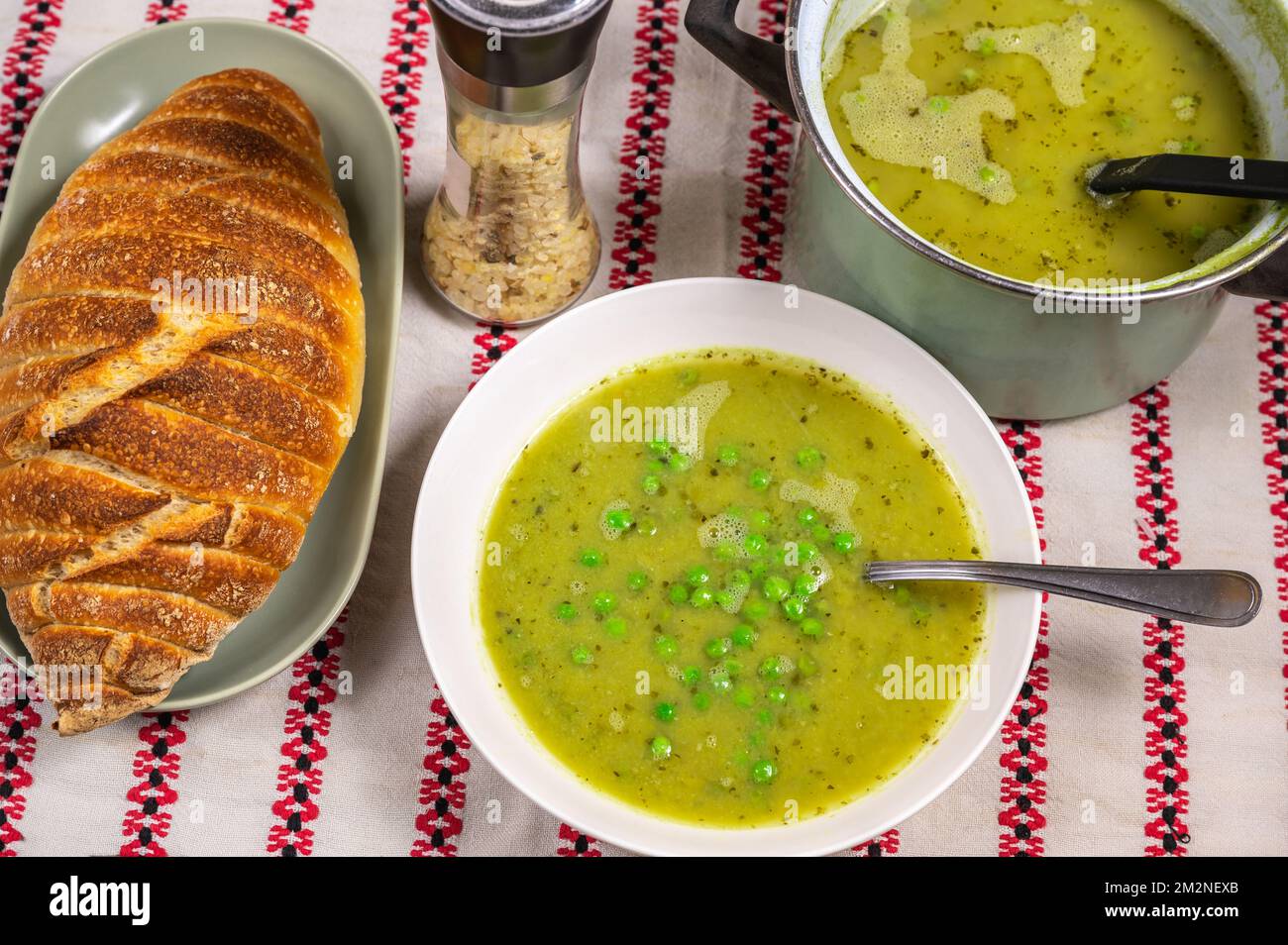 Pea soup in plate and pot, bread and salt shaker on red striped ...