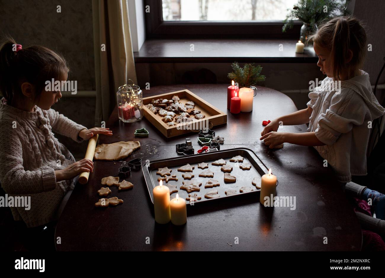 Cute little girls are cooking Christmas gingerbread on a wooden table ...