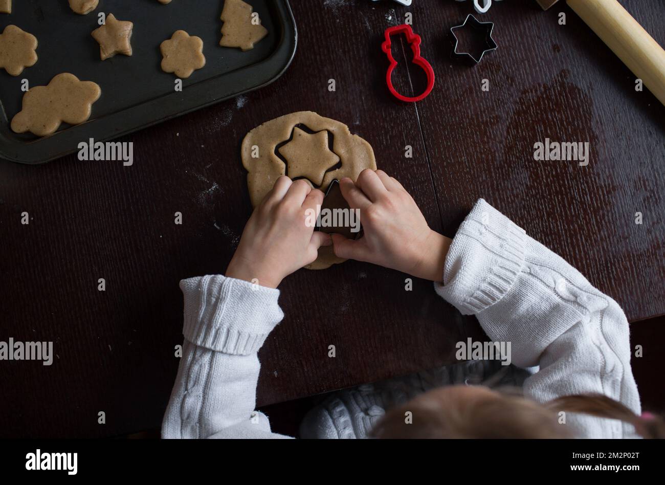 Child cuts cookies. Top view of kids hands with dough, rolling pin and ...