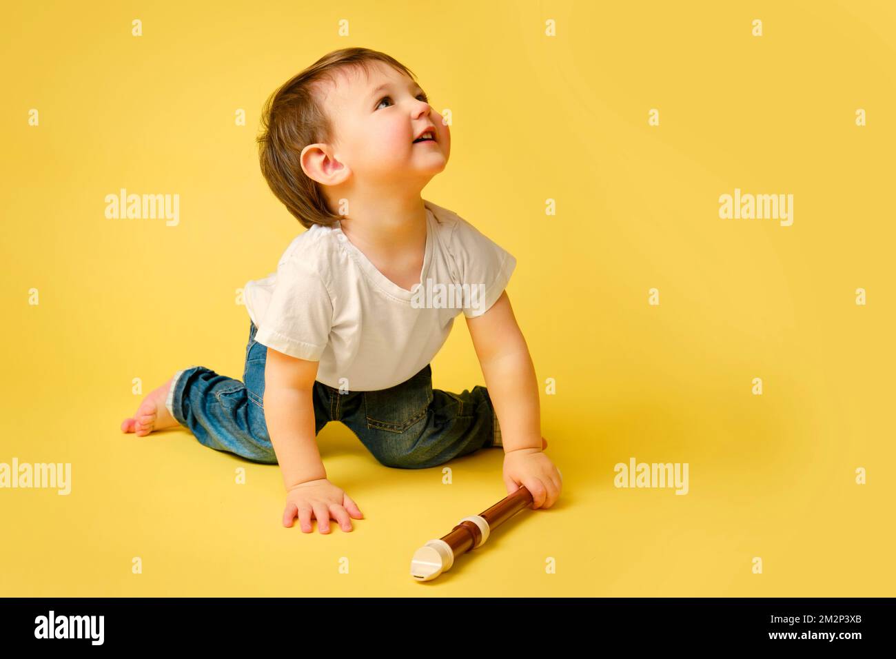 Toddler baby with a flute wind musical instrument on a studio yellow ...