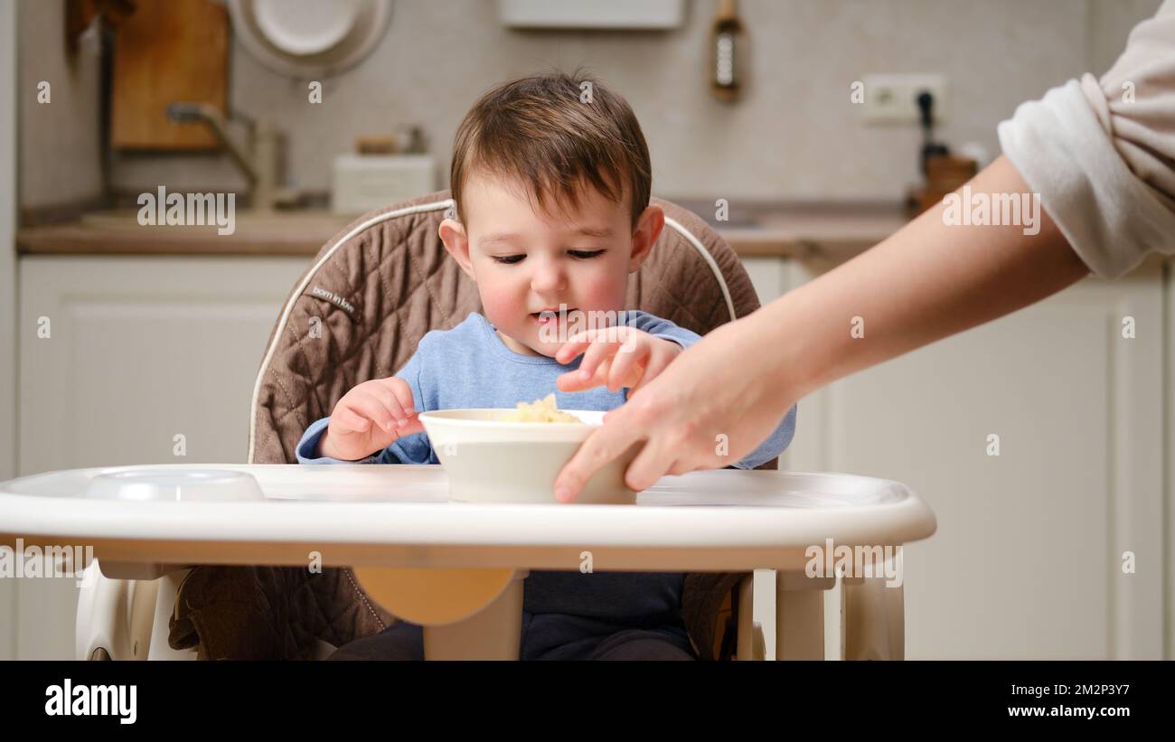 Happy child is eating a grated apple sitting on a kitchen chair ...