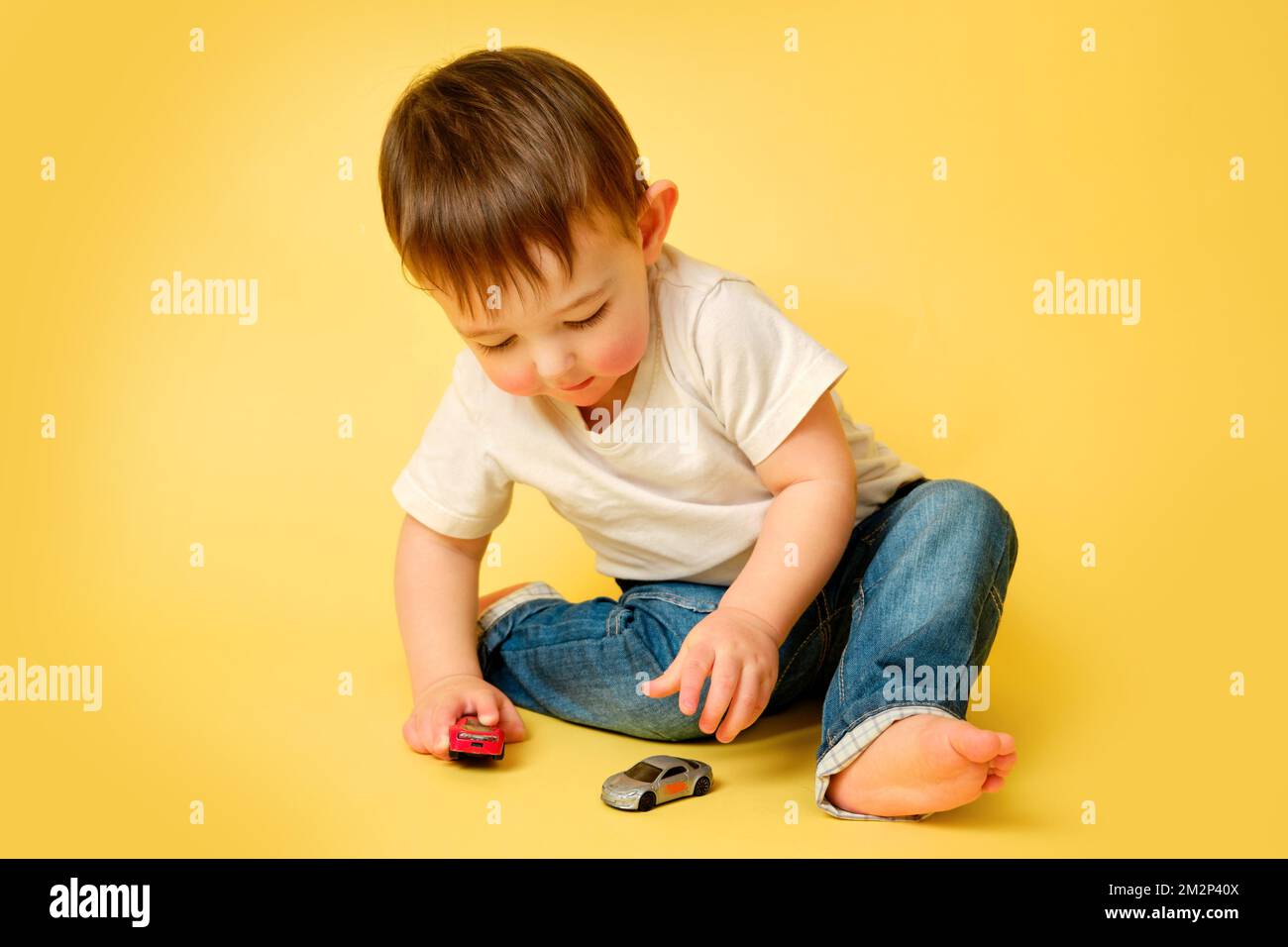 Toddler baby plays with toy cars on a studio yellow background. Happy ...