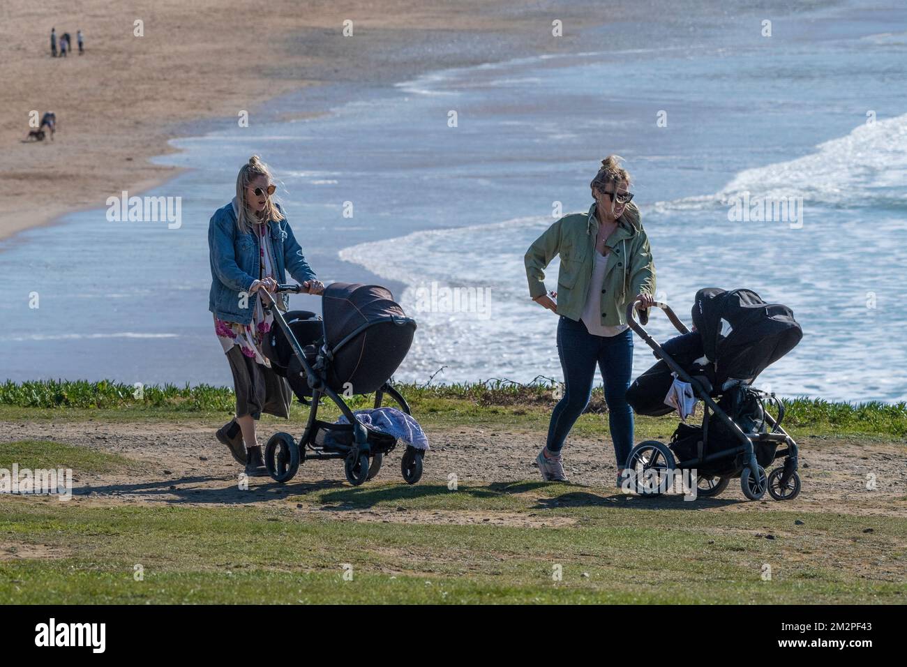 Two young mums pushing their strollers pushchairs on the coast path at ...