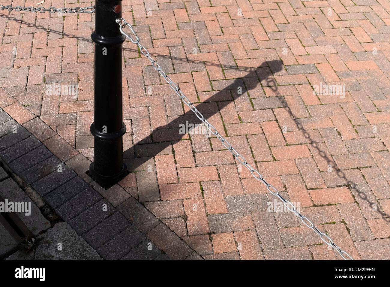 Shadows cast by a bollard and a chain on a driveway in Cornwall in the ...