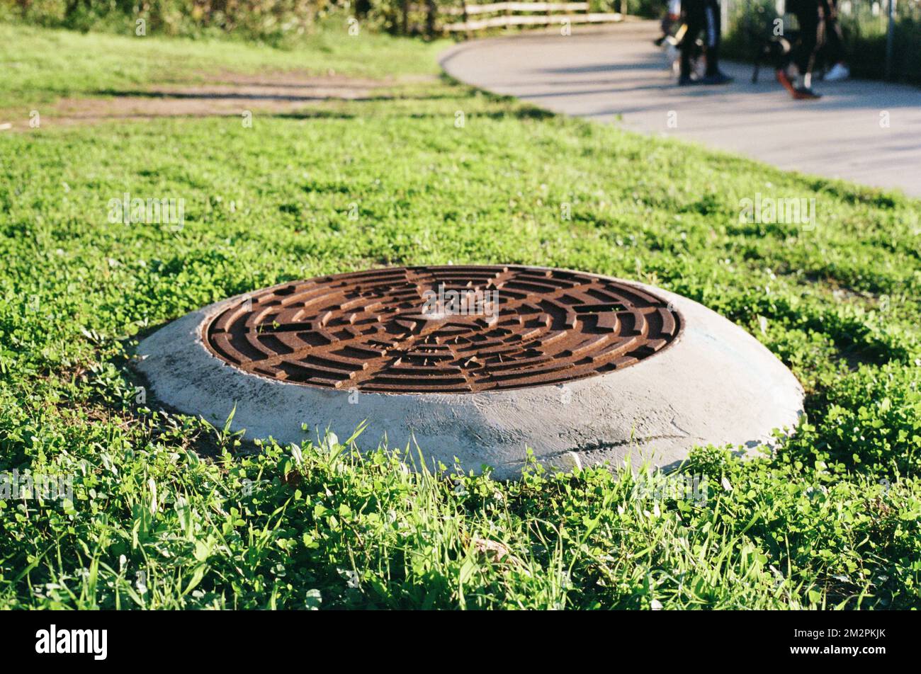 A manhole cover among the green grass of a park by a sidewalk Stock ...