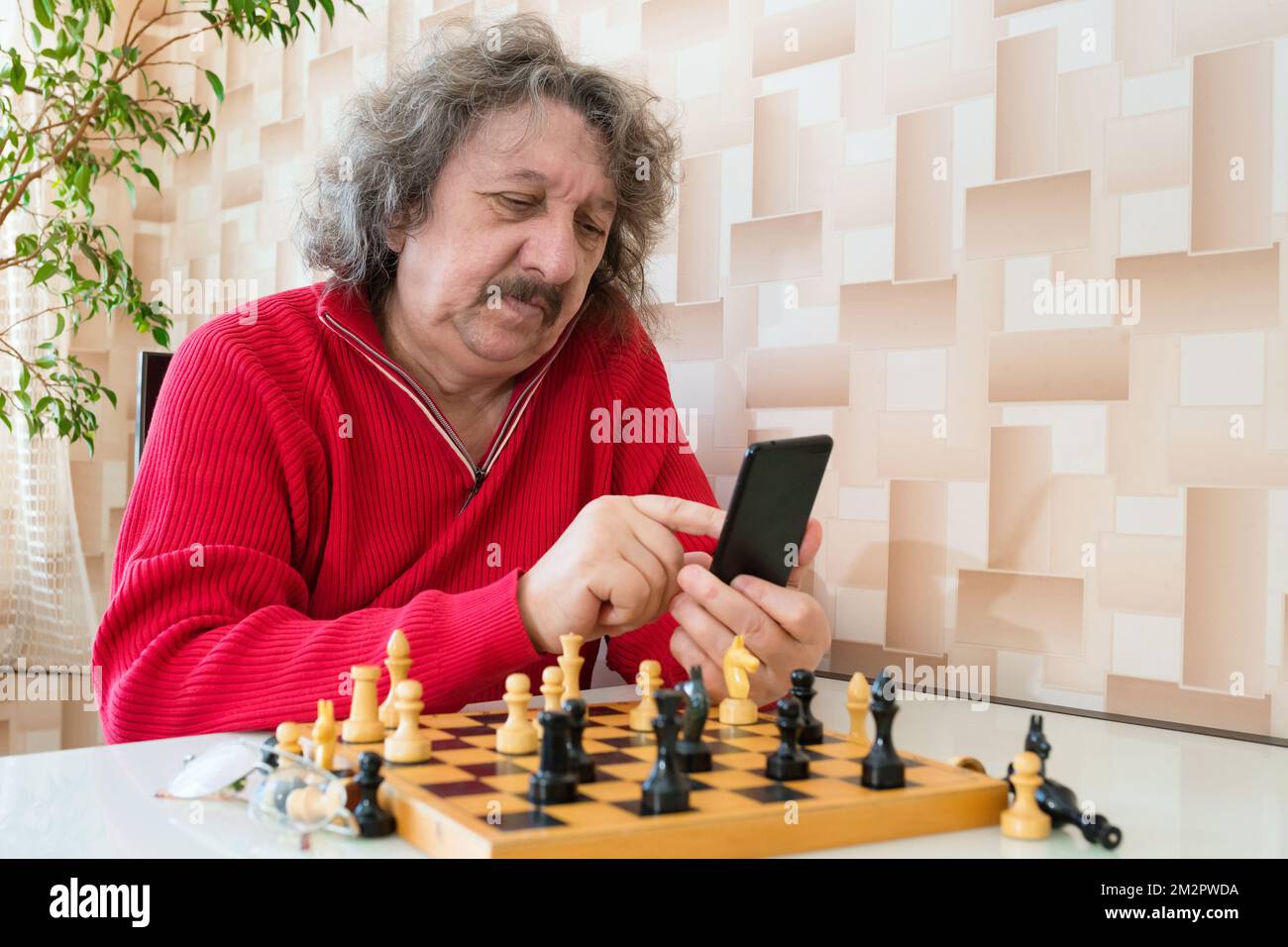 An elderly 60-year or 70-year old man sitting with his phone in hands ...