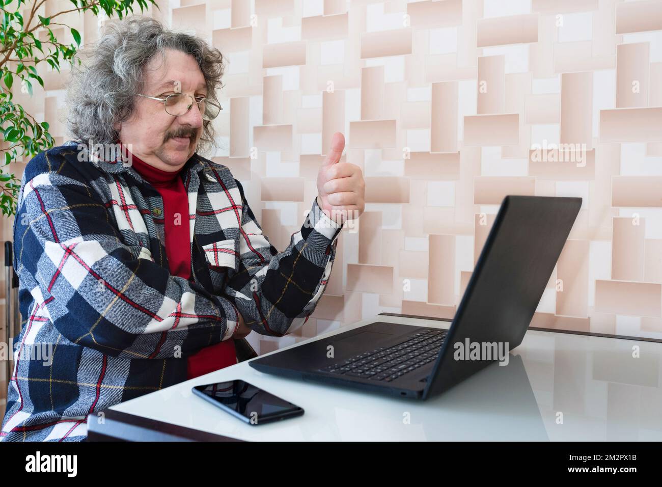 An elderly 70-year old man with a thumb up is talking on the computer ...