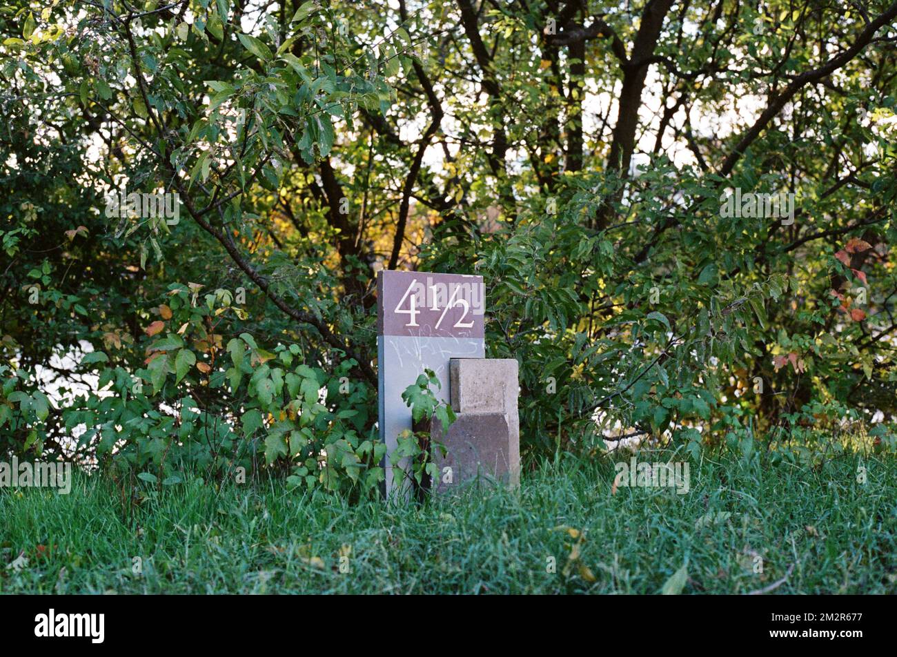 A numbered milestone (4 and half) placed near a shrub in a green field ...