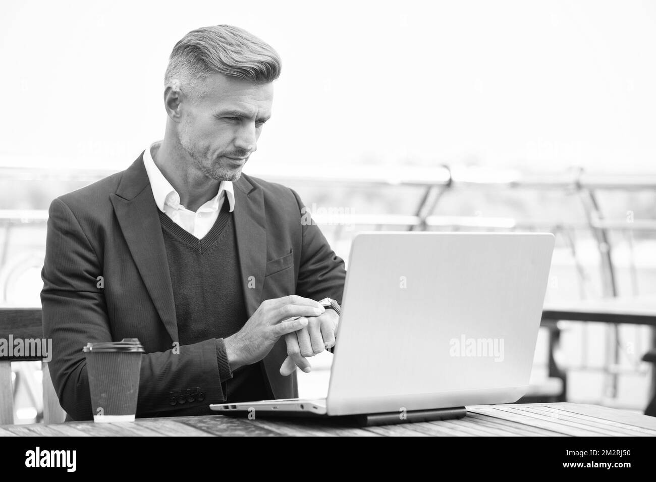 Serious professional man check time on watch working on laptop computer ...