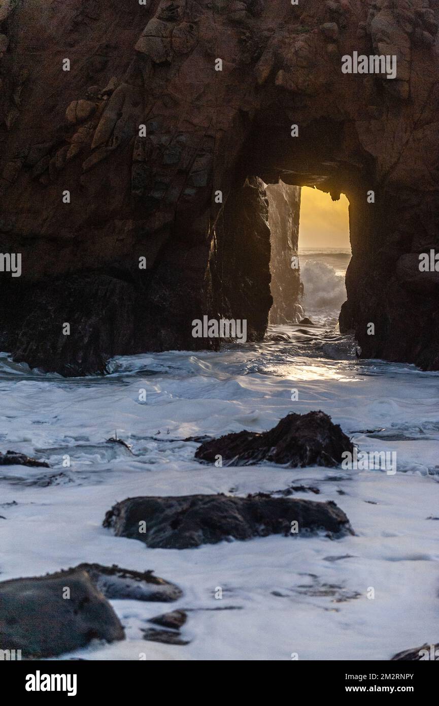 Stormy ocean water flowing through keyhole arch leaiving foam crests on ...