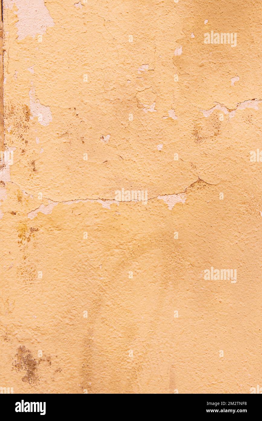 Rough surface of a wall with peeling paint of pale cream yellow color ...