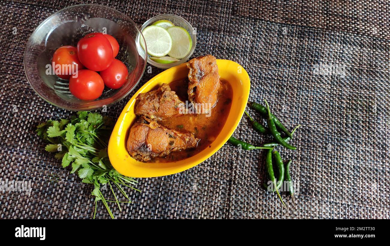 A top view of a chicken curry in a yellow bowl with green and ...