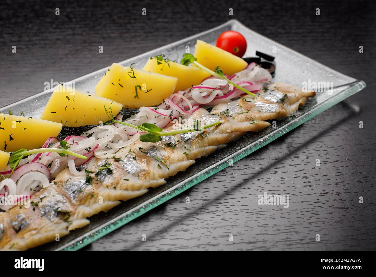 Salted herring with boiled potatoes and herbs, on a dark background ...