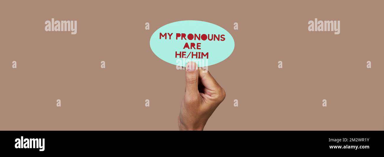 a person has a green sign with the text my pronouns are he, him written ...