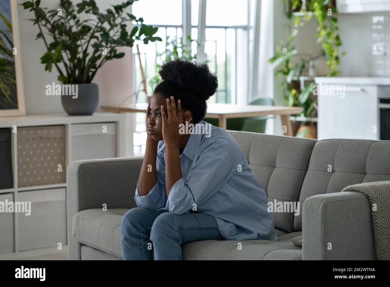 Uninterested discouraged African American woman sits on couch clutching ...