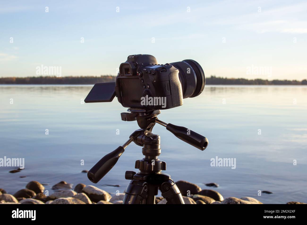 A closeup of a professional camera on a tripod on a rocky shore of a ...