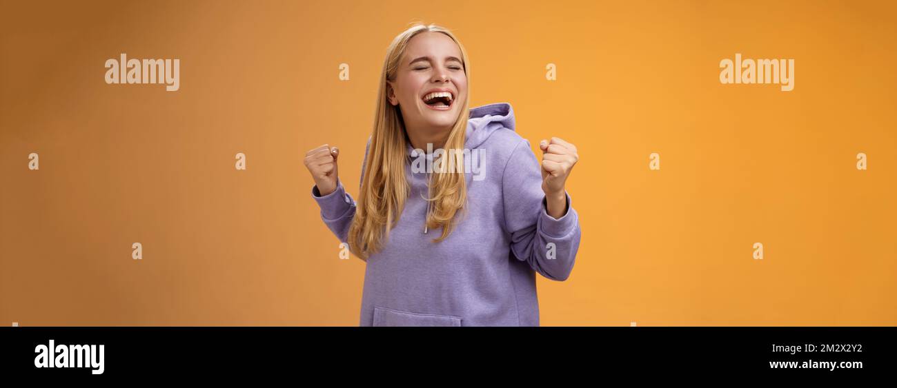 Cute happy triumphing blond european girl in hoodie yelling yes ...