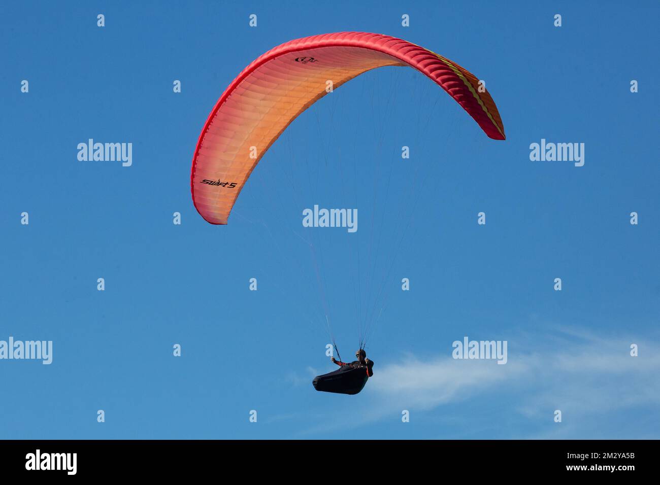 Paraglider flying in front of blue sky with white cloud structures seen ...