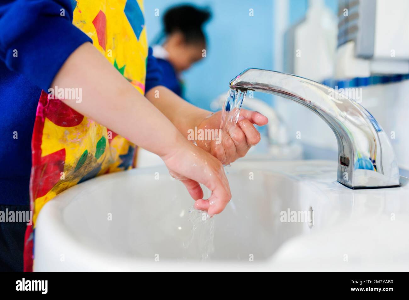Close up of child washing hands in school with child wearing painting ...
