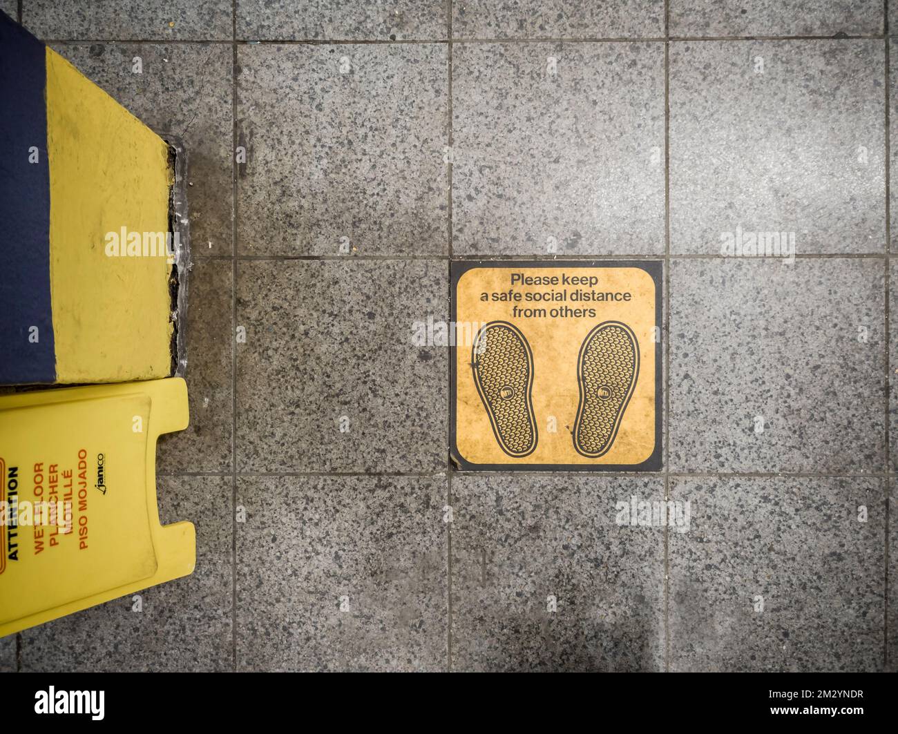 A worn social distancing sticker on the floor of a platform in a subway ...