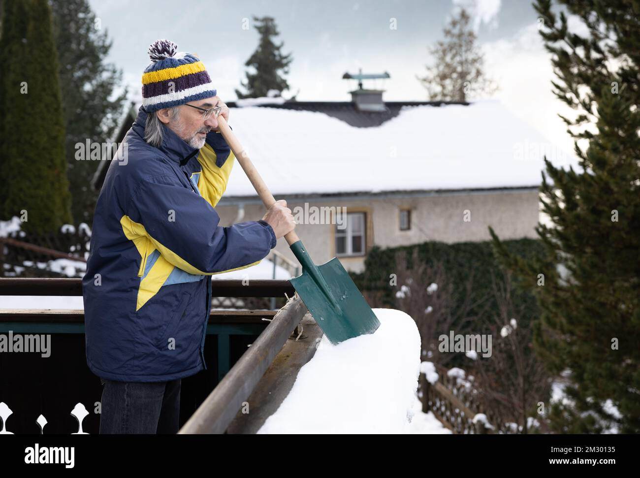 An adult gray-haired man stands on the balcony and cleans snow from the ...