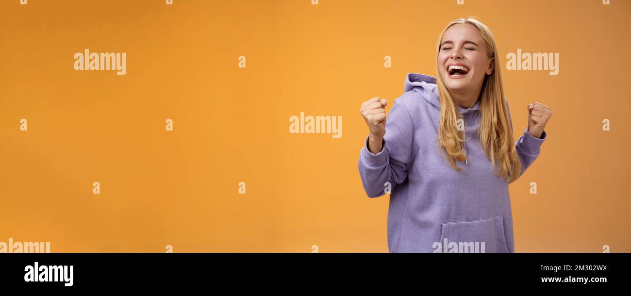 Cute happy triumphing blond european girl in hoodie yelling yes ...
