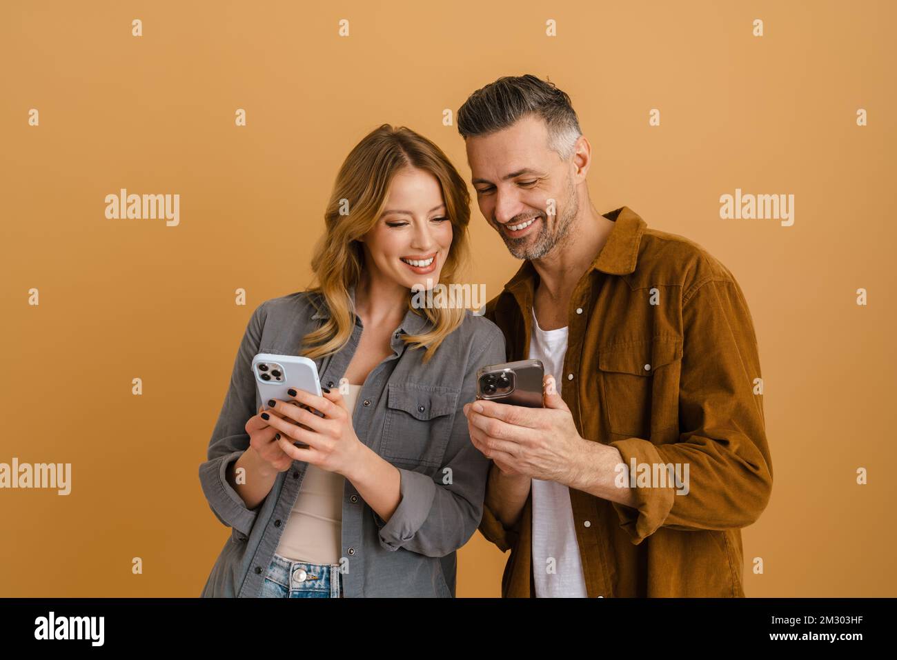 White happy couple using mobile phones while laughing isolated over ...