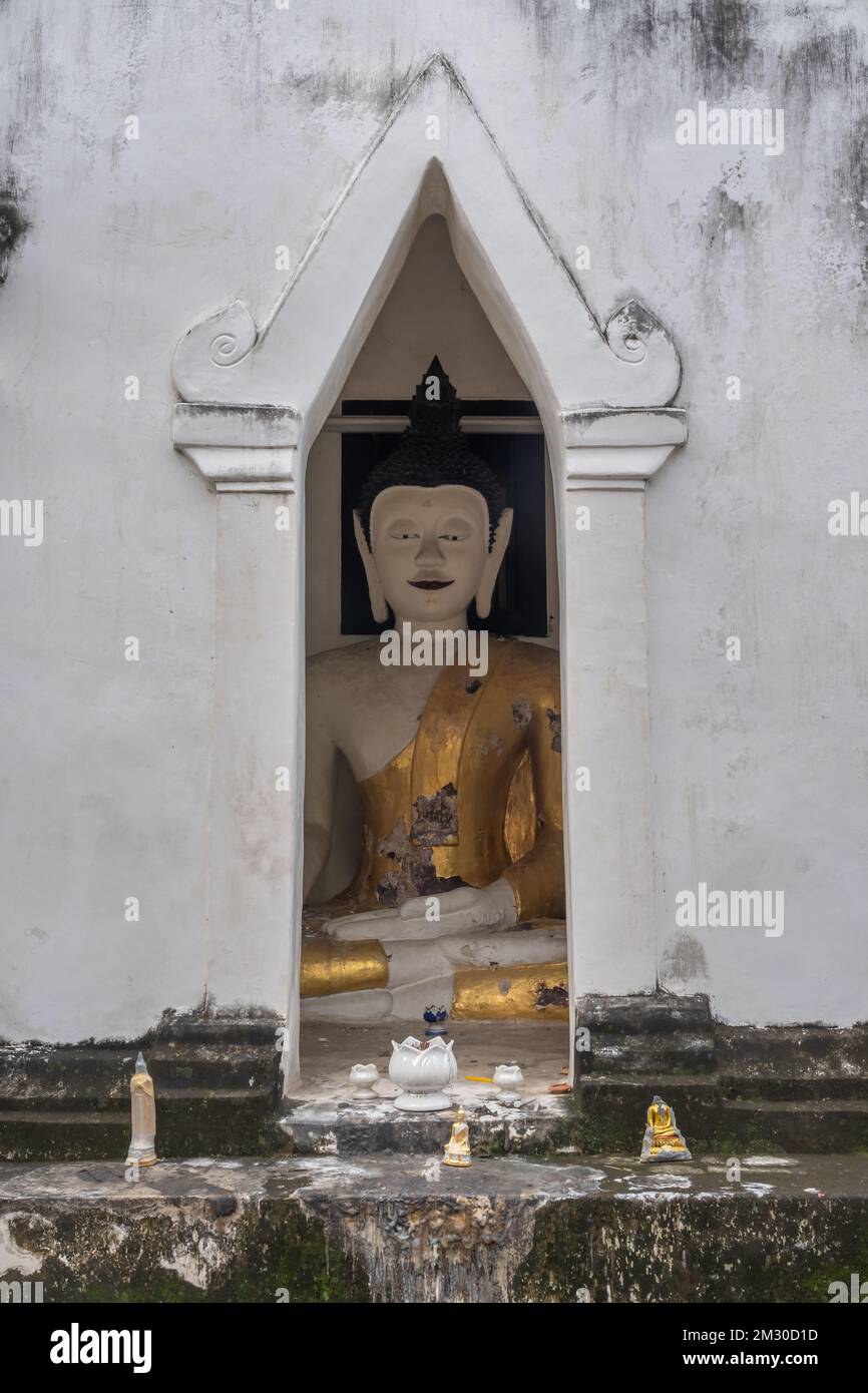 White and gold buddha statue sitting inside niche of ancient stupa at ...