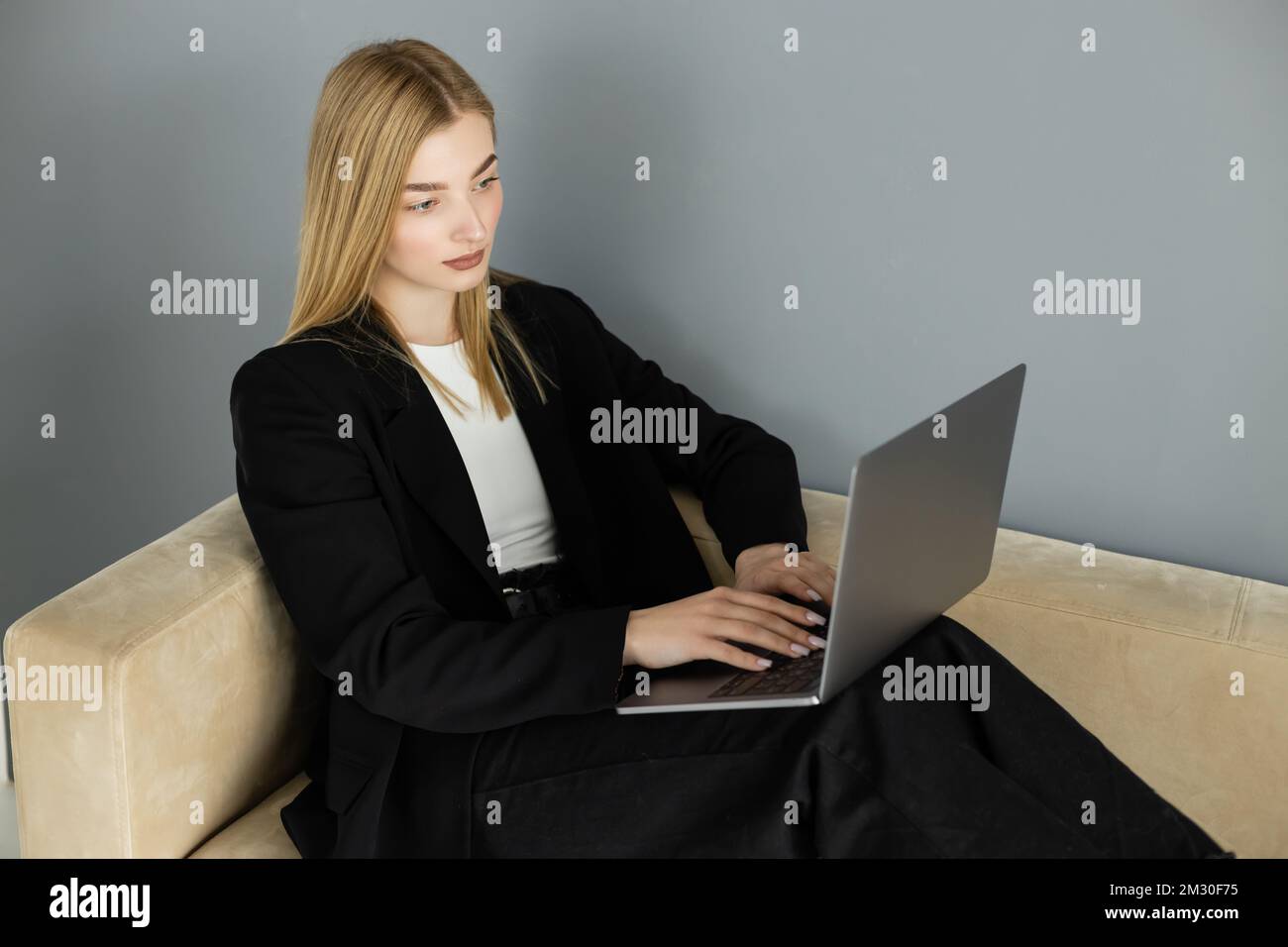 Pretty blonde coach looking at laptop while sitting on beige sofa,stock ...