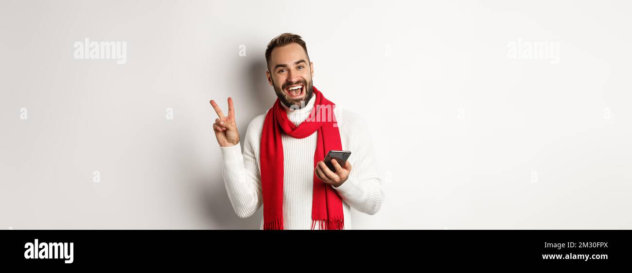 Happy bearded man using smartphone, posing for photo with peace sign ...