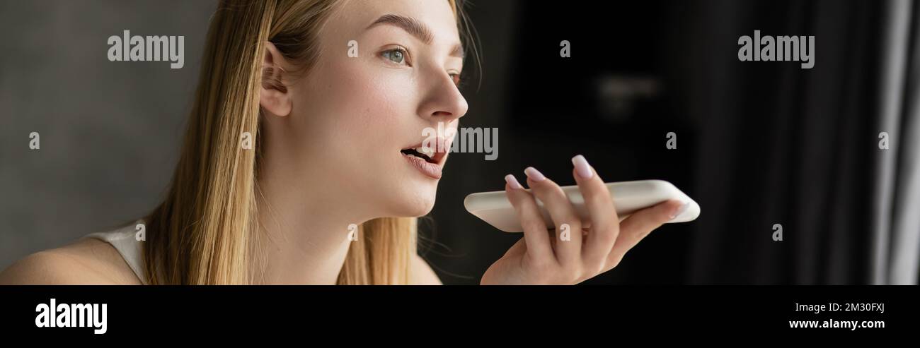Blonde woman recording audio message on smartphone at home, banner ...