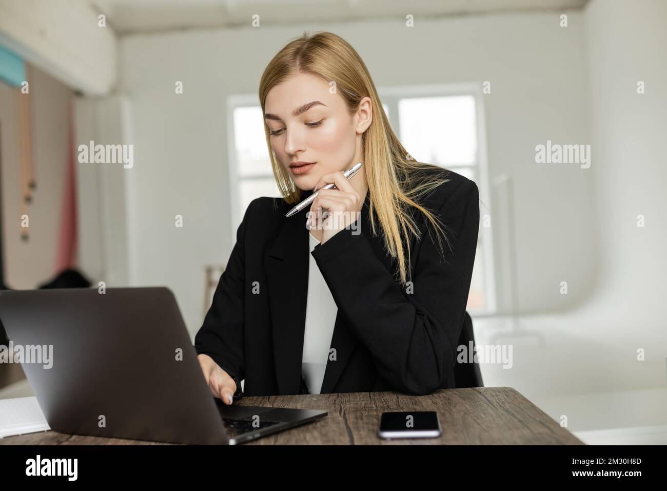 blonde coach holding pen and typing on laptop near smartphone with ...