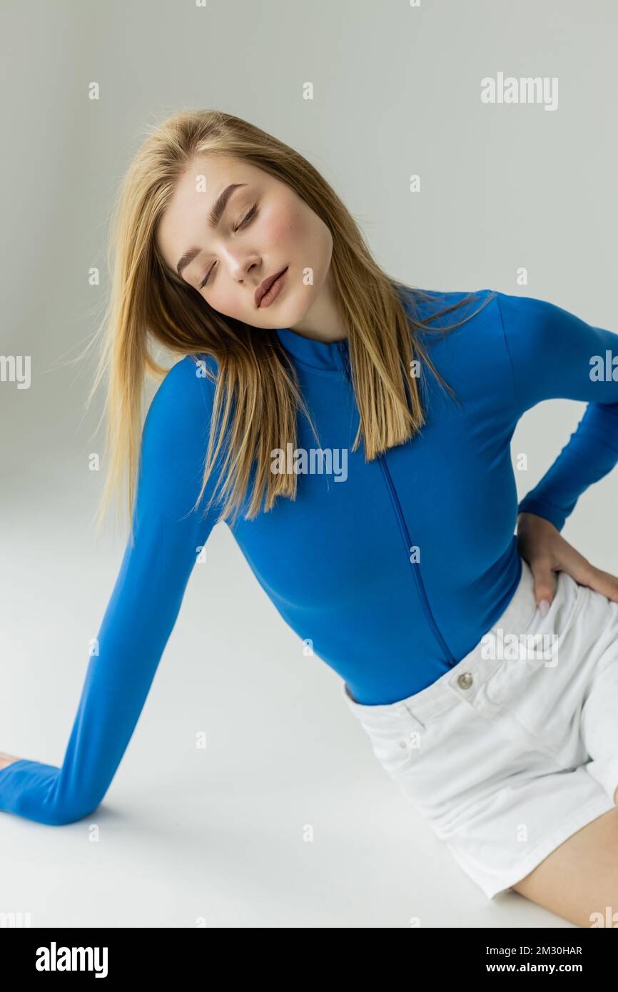 blonde woman in blue zipped turtleneck sitting with closed eyes and ...