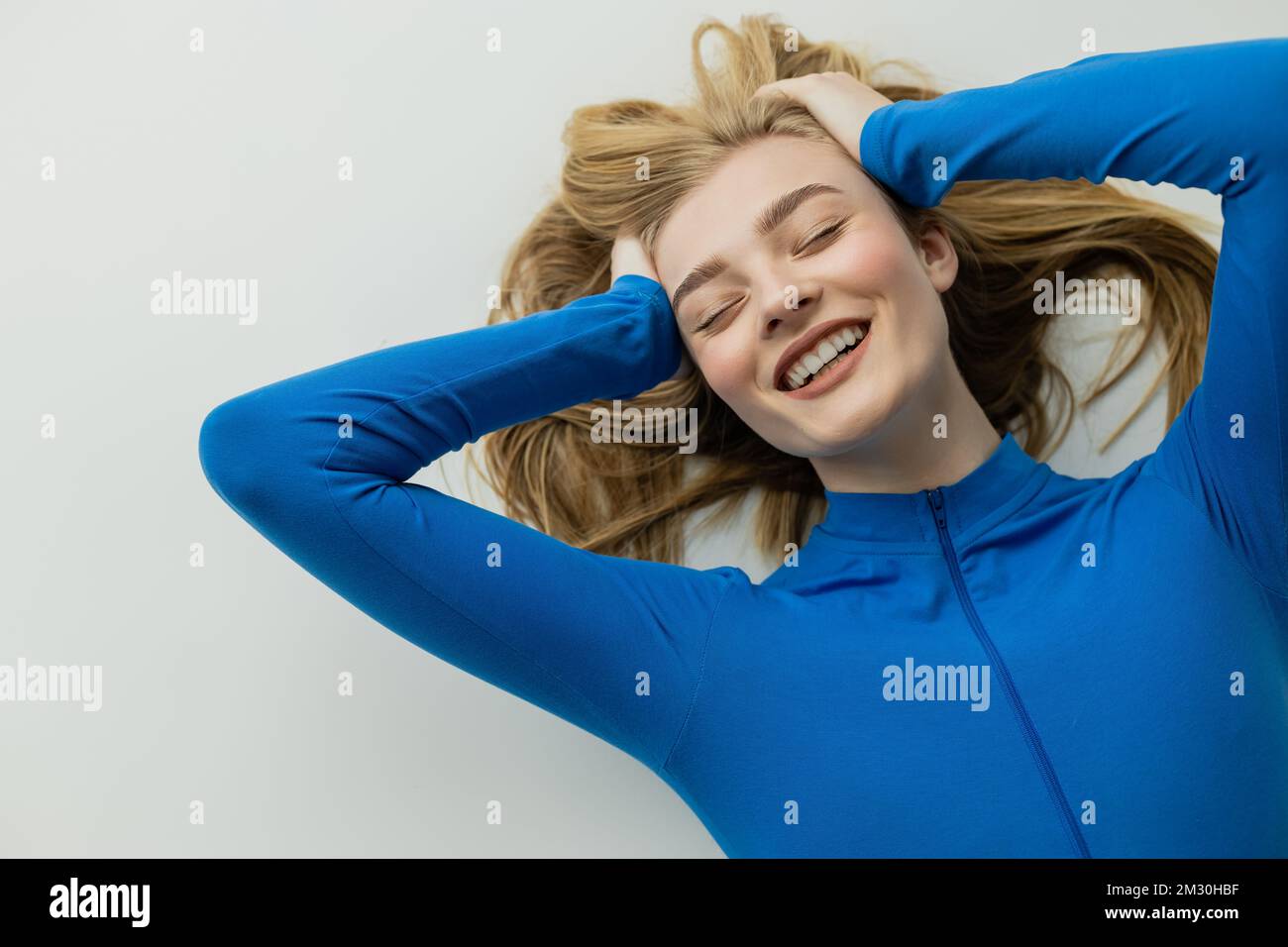 top view of excited woman with closed eyes touching hair and laughing ...
