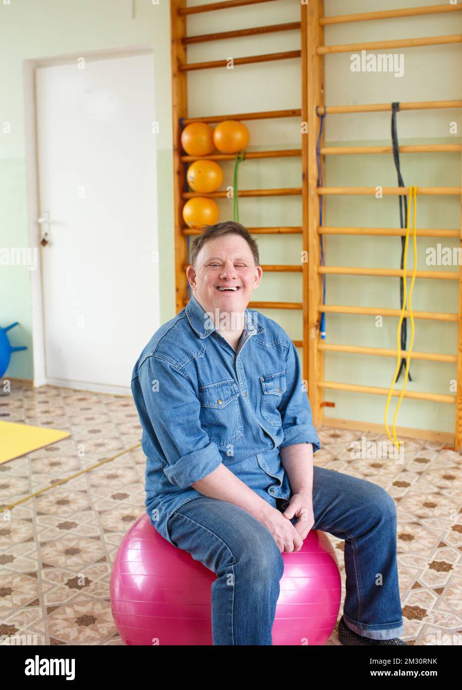 a man with down syndrome sits on a large inflatable ball in a ...